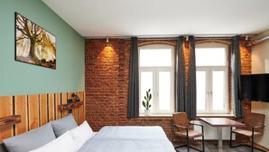 Quarto de hotel com cama, escrivaninha, cadeira, televisão e janela com cortinas.