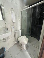 Casa de banho com lavatório, sanita e chuveiro brancos.