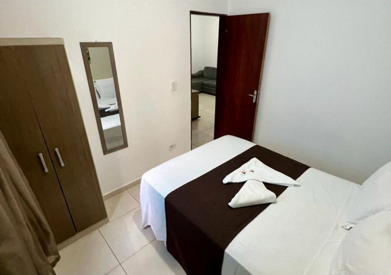 Quarto de hotel com uma cama, um guarda-roupa, um espelho e uma porta.