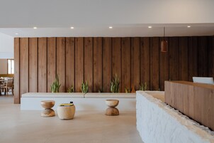 Uma área de recepção moderna com um painel de madeira, um balcão de recepção branco e três banquinhos de madeira.