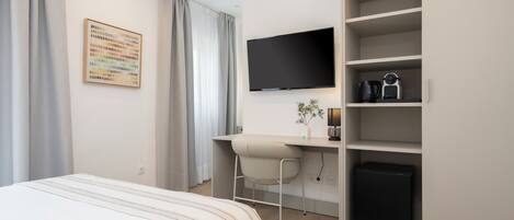 Quarto de hotel com uma cama, uma escrivaninha com cadeira, televisão e guarda-roupa.