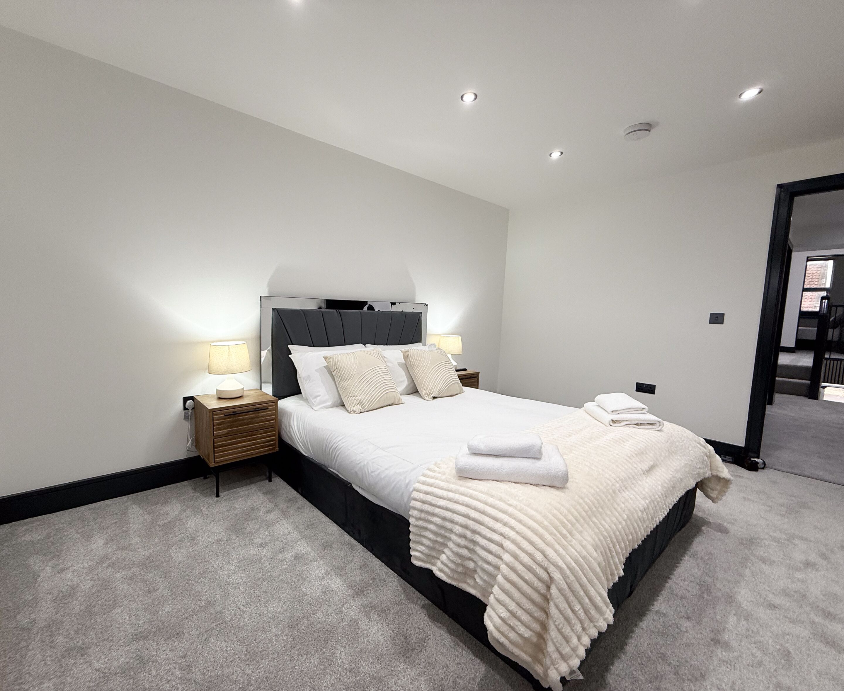Quarto moderno com uma cama grande, abajures e esquema de cores neutras.