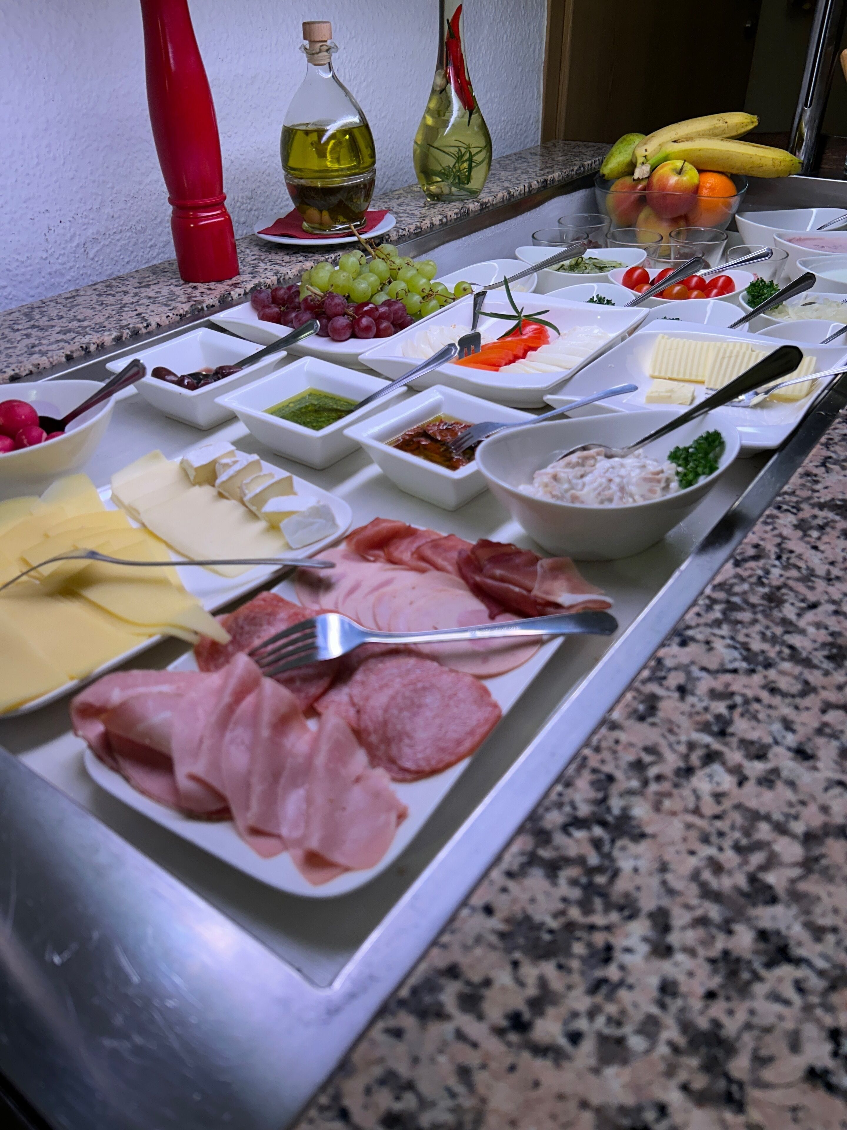 Buffet com diversos alimentos, incluindo queijos, carnes, frutas e acompanhamentos.