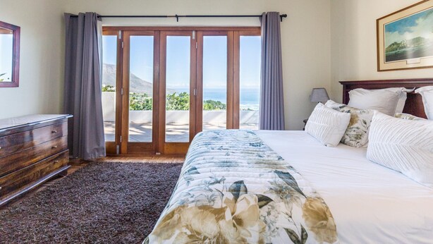 Quarto com uma cama grande, cômoda, ventilador de teto e vista para o oceano através de uma porta de vidro deslizante.