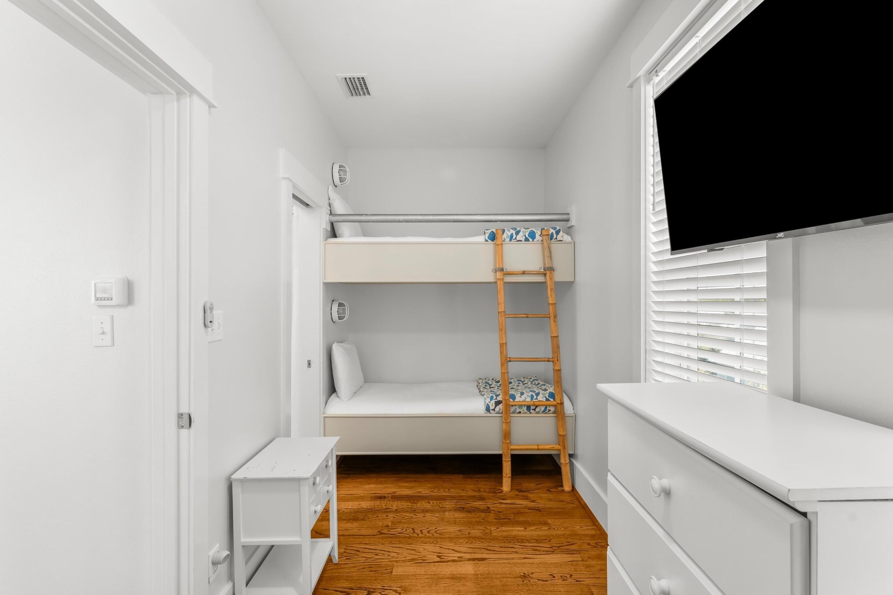 Quarto compacto com beliche, uma pequena escrivaninha e televisão.