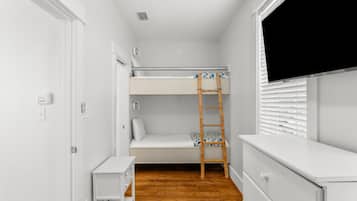 Quarto compacto com beliche, uma pequena escrivaninha e televisão.