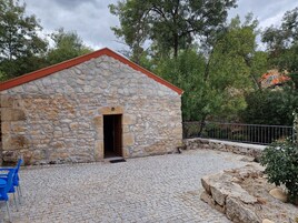 Um edifício de pedra com telhado vermelho, um pátio pavimentado e uma cerca de metal.