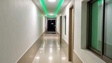 Um corredor com piso ladrilhado brilhante, iluminação embutida e uma porta no final.