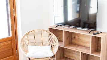 Quarto com estante de TV de madeira, televisão de tela plana, cadeira de vime e almofada branca.