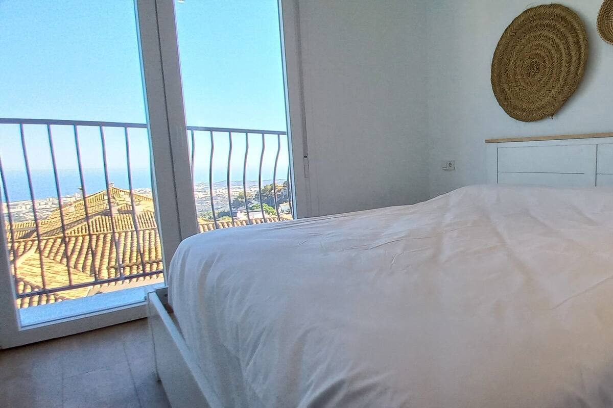Quarto com uma cama, vista através de uma varanda e três decorações de parede trançadas.