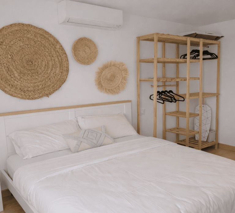 Quarto com cama, estante de madeira e dois painéis de parede trançados.