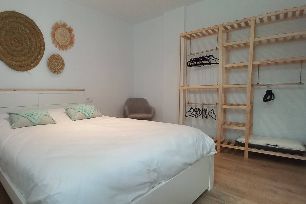 Quarto com cama, uma cadeira, prateleira de madeira com roupas e decorações nas paredes.