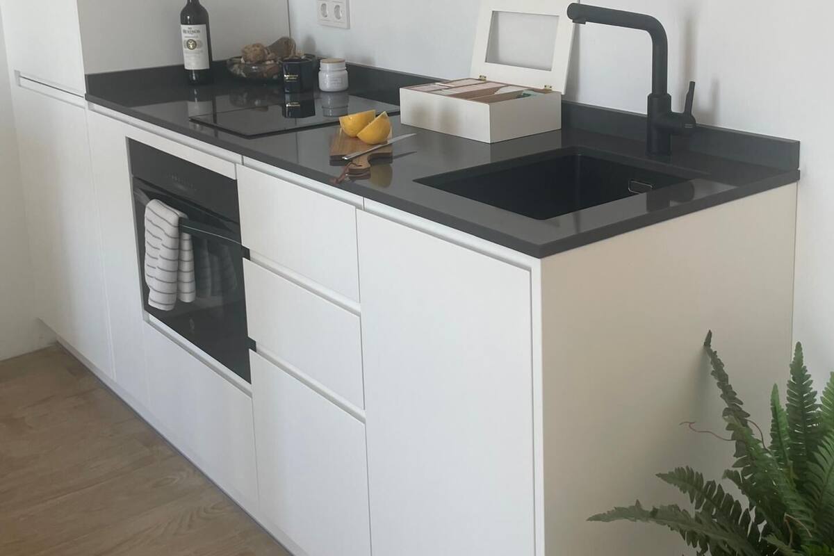 Uma cozinha moderna com bancada preta, armários brancos, lava-louças embutida e uma pia.