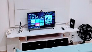 Uma sala de estar moderna com televisão de tela plana, um rack branco, um ventilador preto e um sofá verde-água.