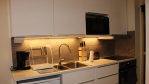 Uma cozinha moderna com armários brancos, uma pia de aço inoxidável, forno embutido e cafeteira.