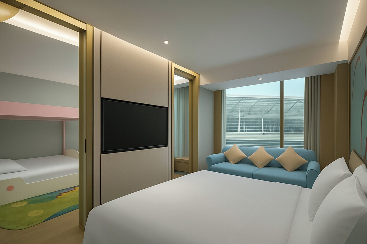 Quarto de hotel com cama grande, sofá, televisão e janela com vista para a cidade.