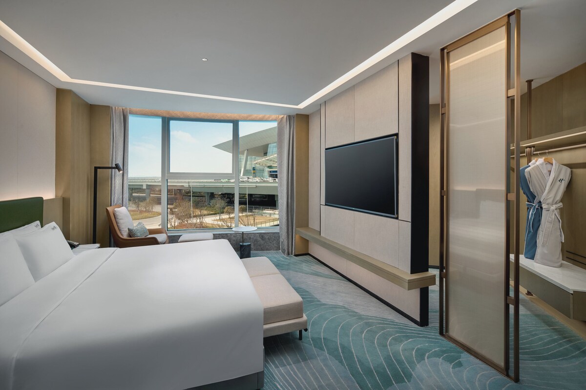 Quarto de hotel moderno com uma cama grande, área de estar, TV e vista para o exterior.