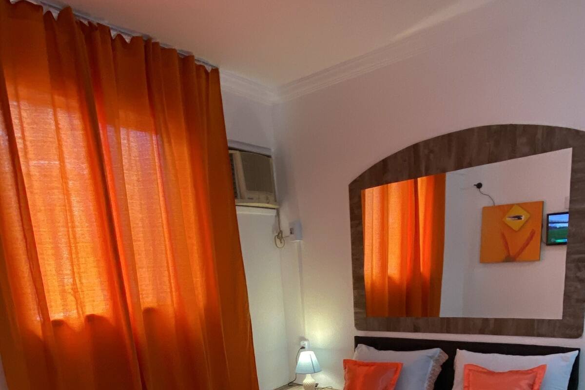 Quarto de hotel com cama, mesa de cabeceira, abajur e televisão.