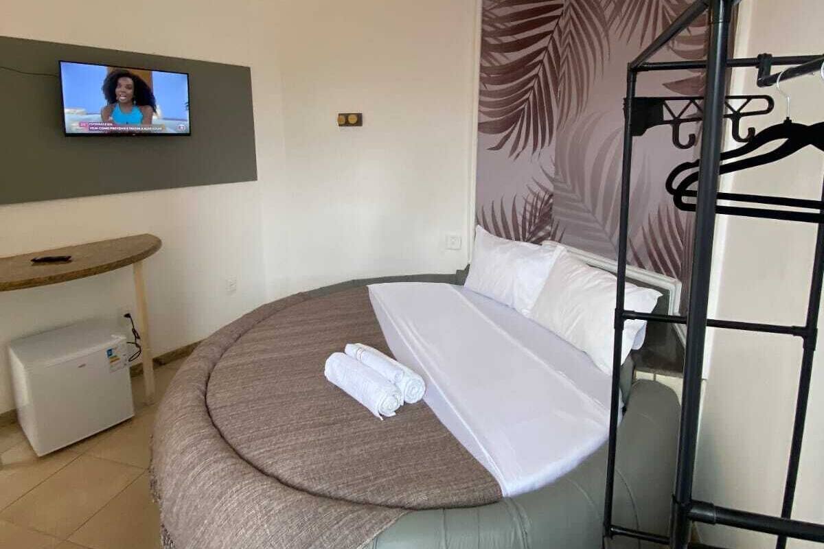 Quarto moderno com cama redonda, televisão na parede, secretária pequena e mural no teto.