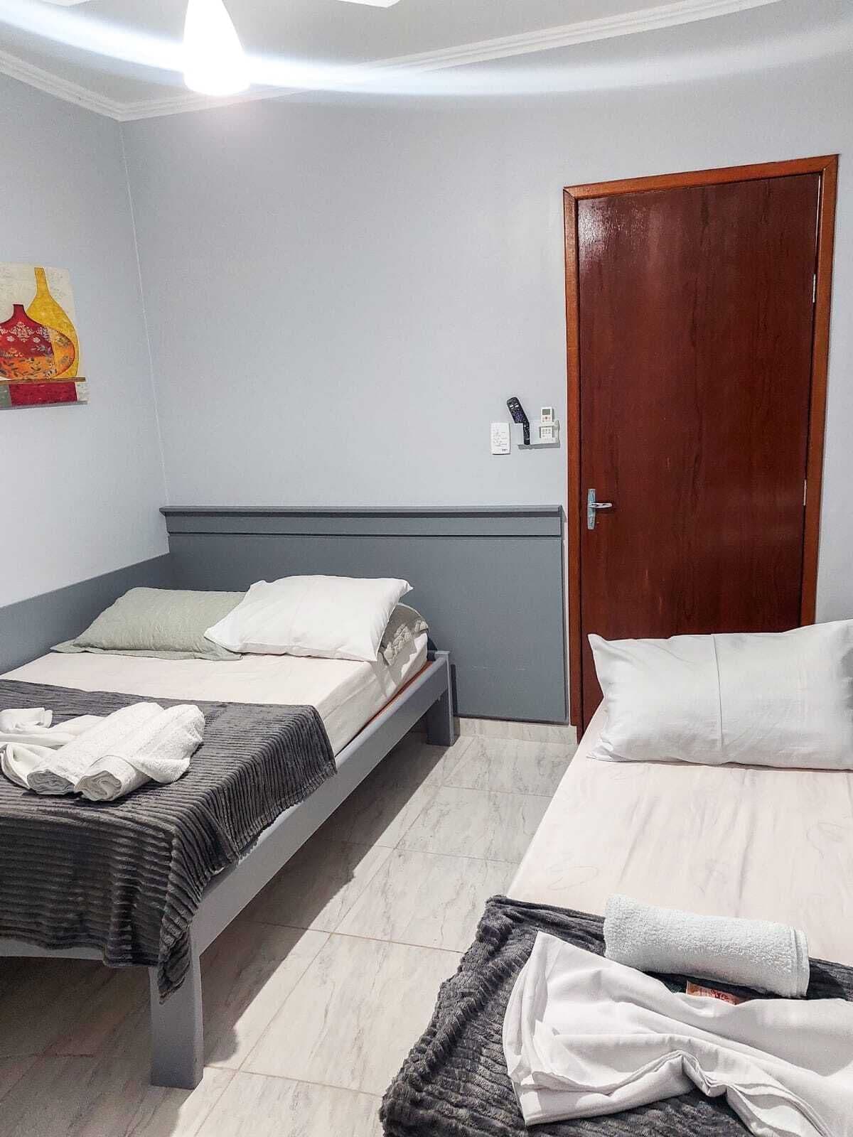 Quarto com duas camas de solteiro, porta de madeira, telefone fixado na parede e um vaso decorativo.