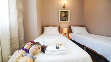Quarto de hotel com duas camas, uma mesa de cabeceira com abajur, um quadro na parede e uma janela com cortinas.