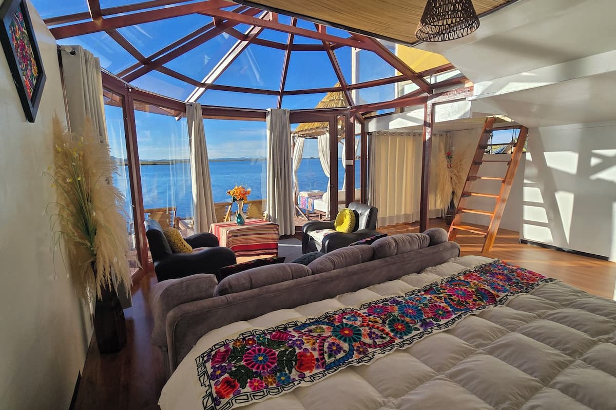 Quarto com cama grande, vista para o mar, teto de madeira e escada.