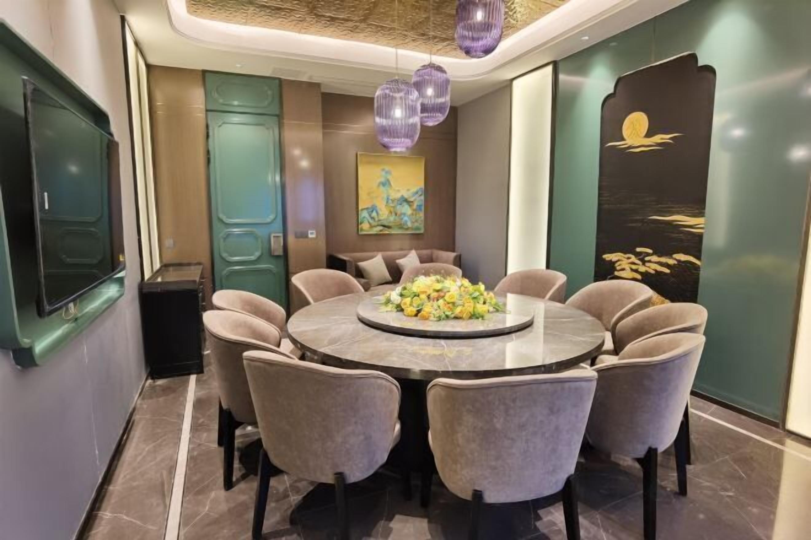 Uma área de refeições moderna com uma mesa redonda, cadeiras estofadas em cinza e iluminação decorativa.