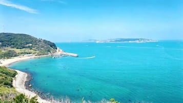 Paisagem costeira com praia, mar azul-turquesa e formações terrestres ao longe.
