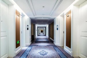 Corredor de hotel com piso revestido de carpete, portas em ambos os lados e um corredor central que leva a uma porta no final.