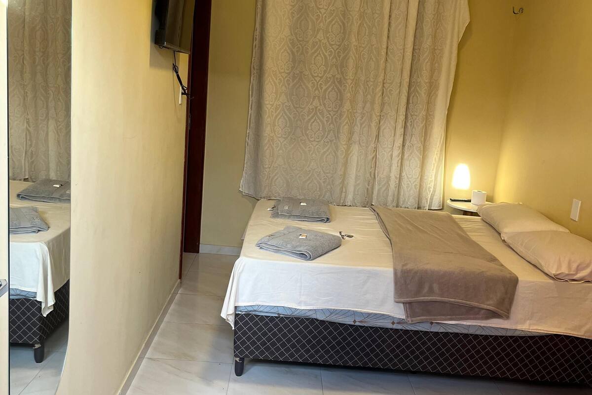 Quarto com cama, mesa de cabeceira, espelho, ar condicionado fixado na parede e cortina.