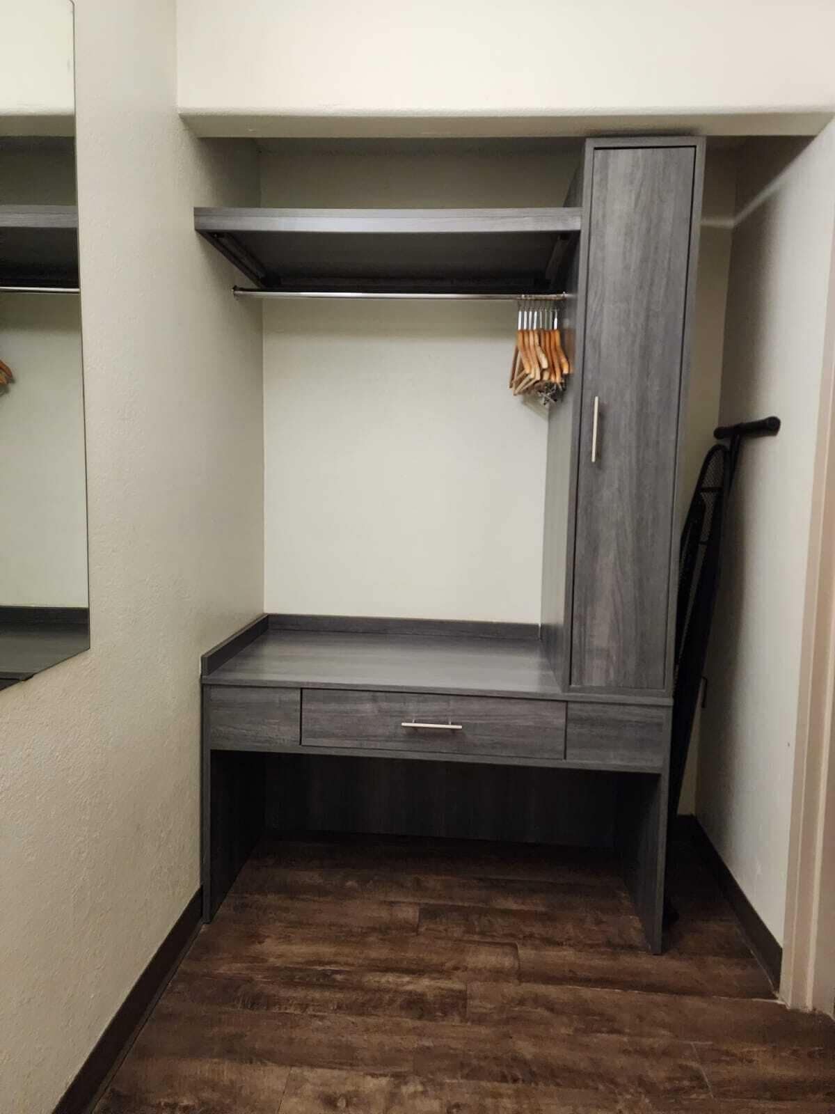 Quarto compacto com escrivaninha de madeira escura, guarda-roupa e espelho.
