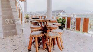 Um terraço com uma mesa de madeira no centro, rodeada por taburetes, uma escadaria e plantas em vasos.