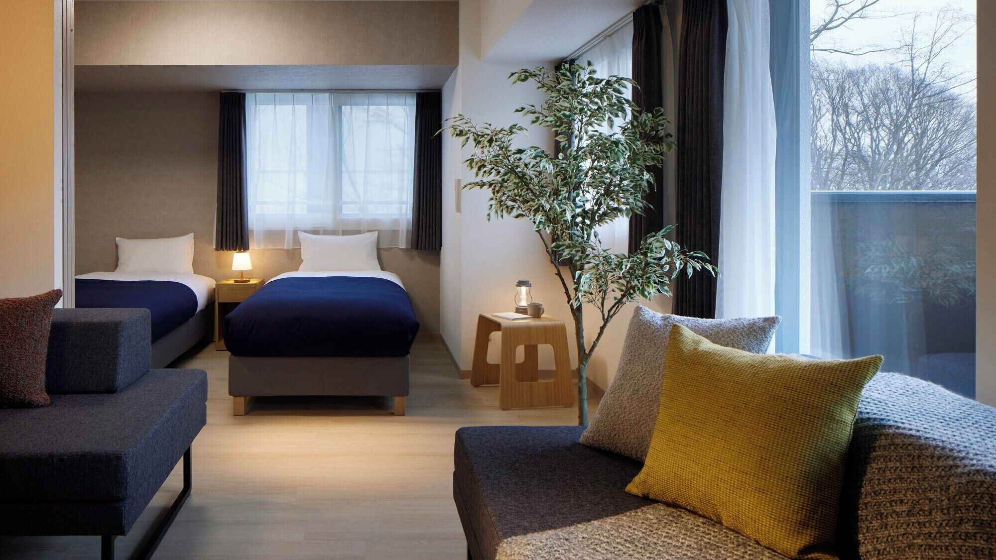 Quarto de hotel moderno com uma cama grande, um sofá, uma mesinha e um vaso de planta.