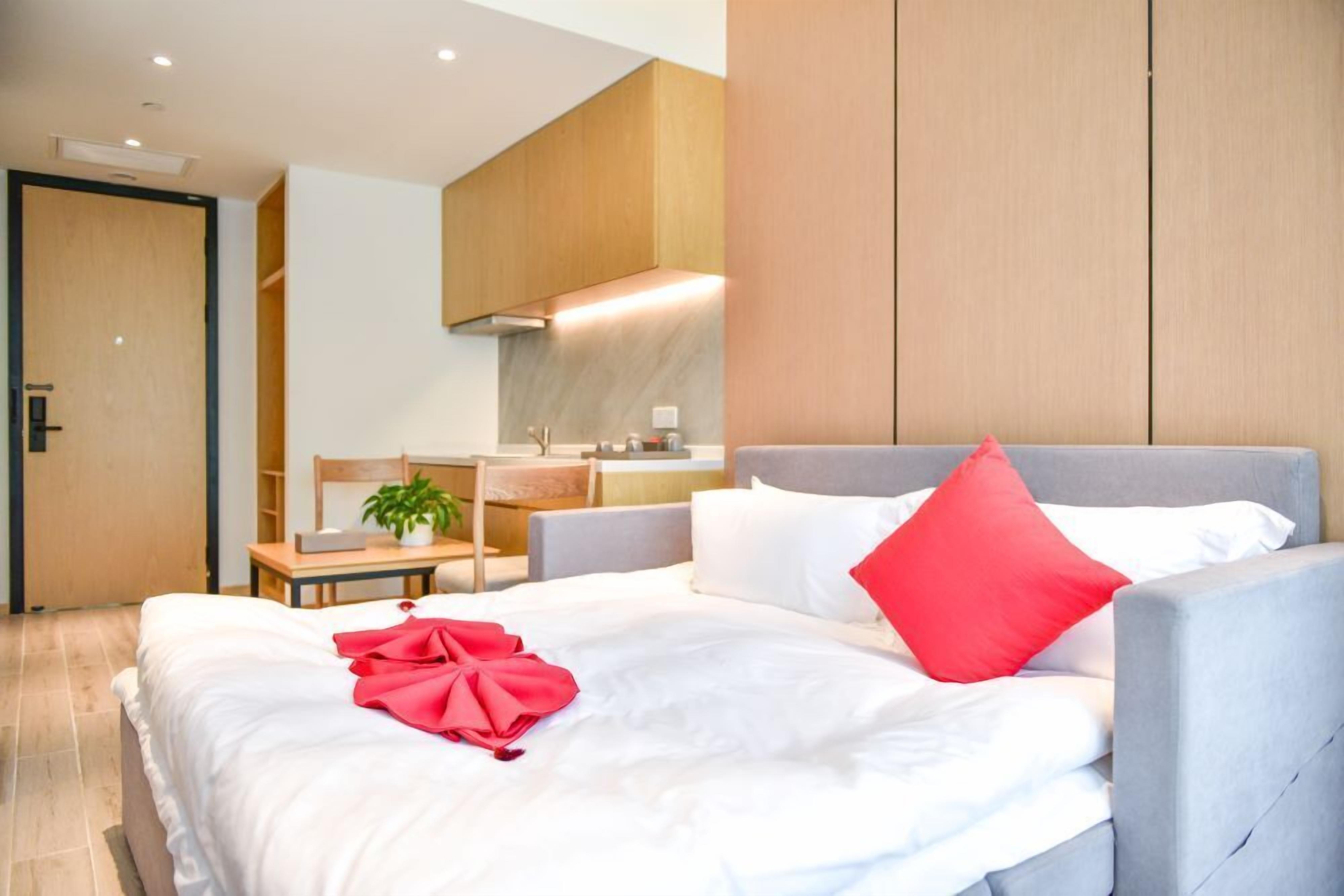 Quarto de hotel moderno com uma cama grande, uma mesa de trabalho e uma cozinha compacta.