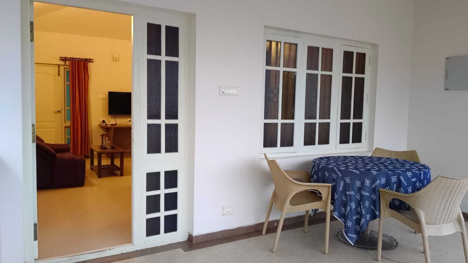 Quarto com uma mesa de jantar, duas cadeiras, uma janela com vários painéis e uma porta que dá para outro cômodo.