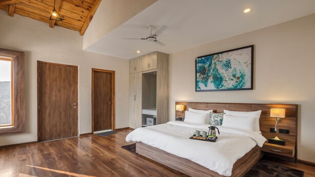 Quarto espaçoso com uma cama grande, piso de madeira, ventilador de teto e um quadro na parede.