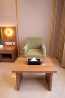 Um quarto com uma mesa de madeira, um sofá verde e uma mesa de cabeceira com uma luminária.