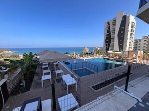 Piscina no terraço com espreguiçadeiras e guarda-sóis, com vista para a paisagem urbana costeira.