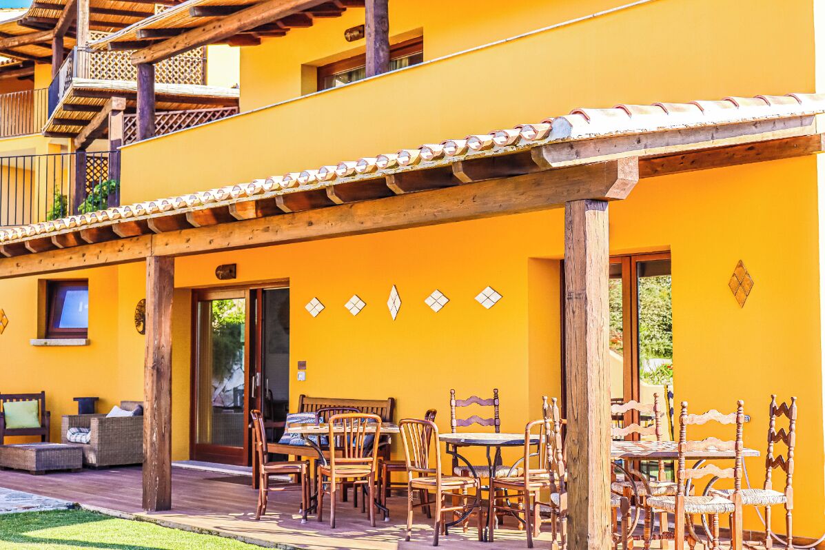 Um edifício amarelo com mesas ao ar livre e uma pérgula de madeira.