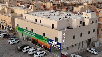 Um hotel com telhado plano, vários espaços de estacionamento e uma placa a indicar 'Alma Central Markets'.