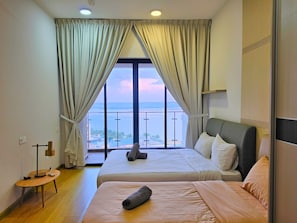 Quarto de hotel com duas camas, uma mesinha e vista para o mar.