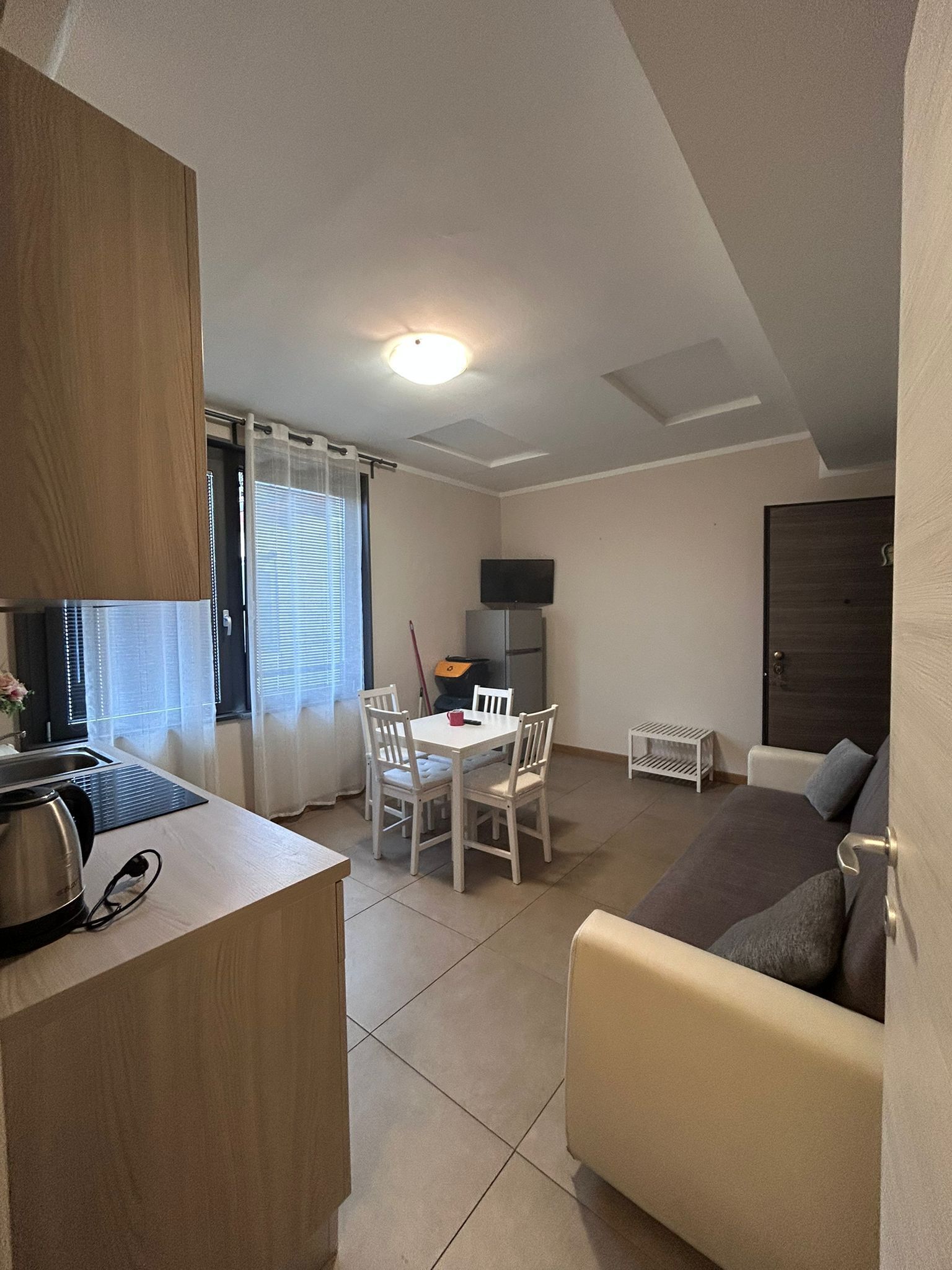 Um espaço de estar compacto com cozinha compacta, área de refeições com mesa e cadeiras, sofá e TV fixada na parede.