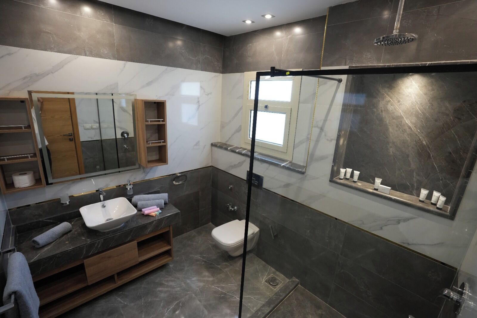 Uma casa de banho moderna com um espelho grande, um chuveiro, uma sanita e um lavatório com exaustor e porta-toalhas.