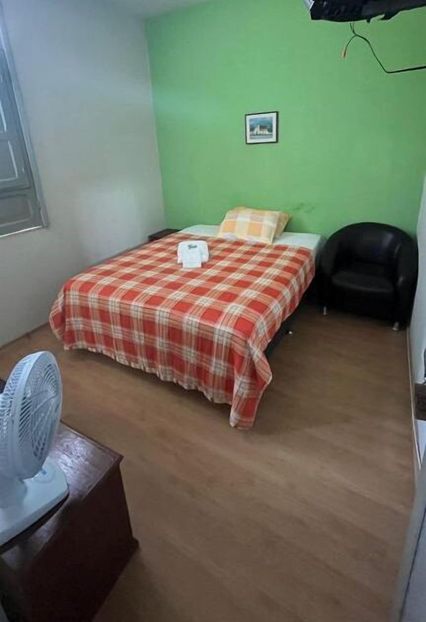 Um quarto com uma cama, uma cadeira e um ventilador.