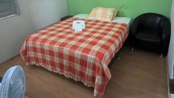 Um quarto com uma cama, uma cadeira e um ventilador.