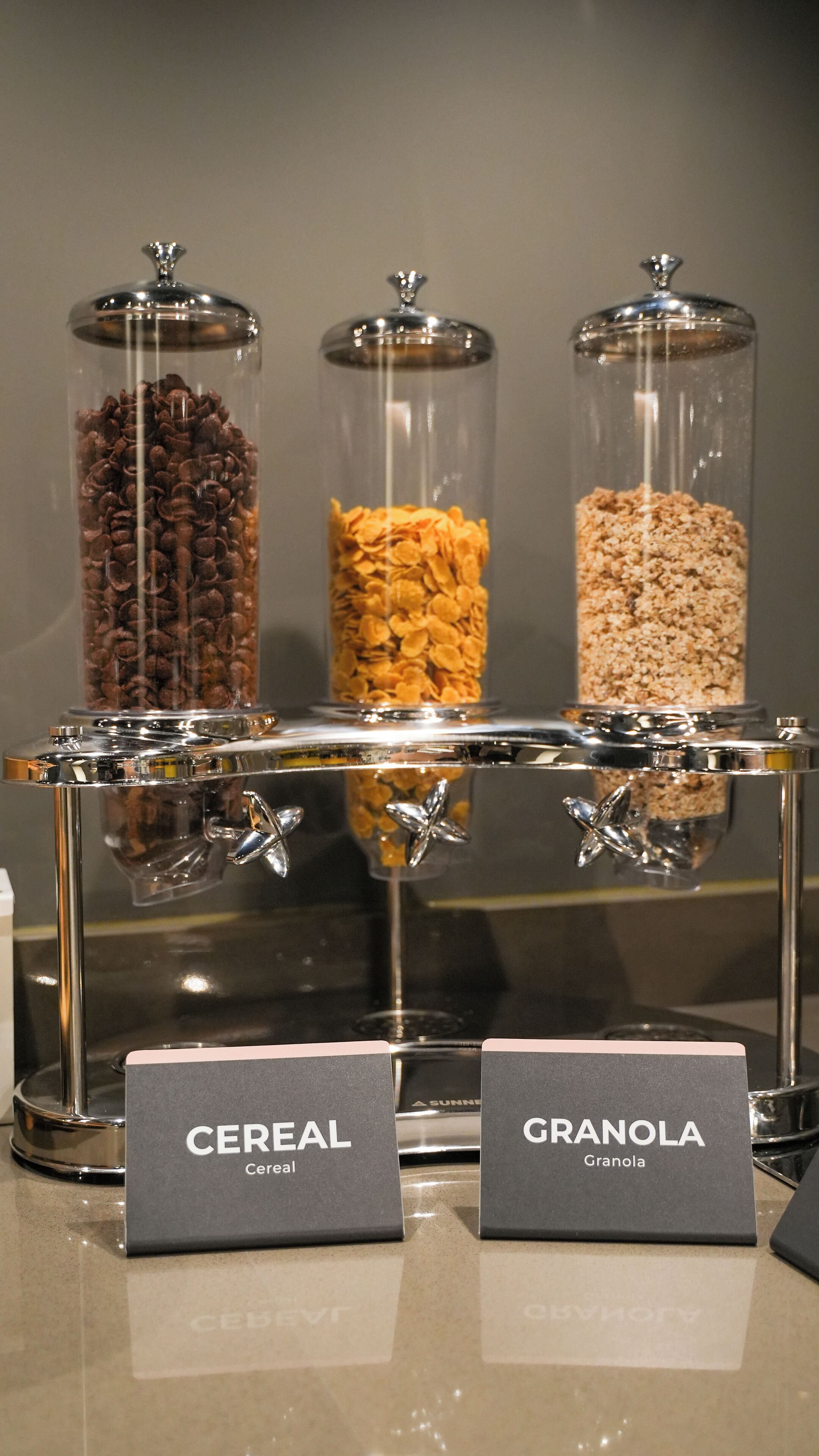 Exposição de granola e cereais em recipientes de vidro com etiquetas.