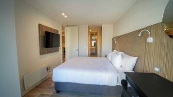 Quarto de hotel moderno com uma cama grande, televisão de tela plana na parede, mesa de cabeceira e escrivaninha com cadeira.