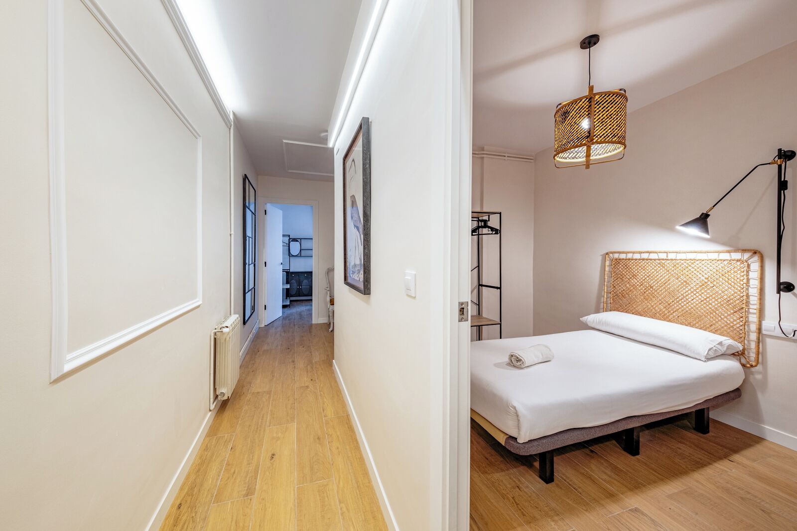 Um corredor estreito que leva a um quarto com uma cama, um candeeiro suspenso e um radiador.