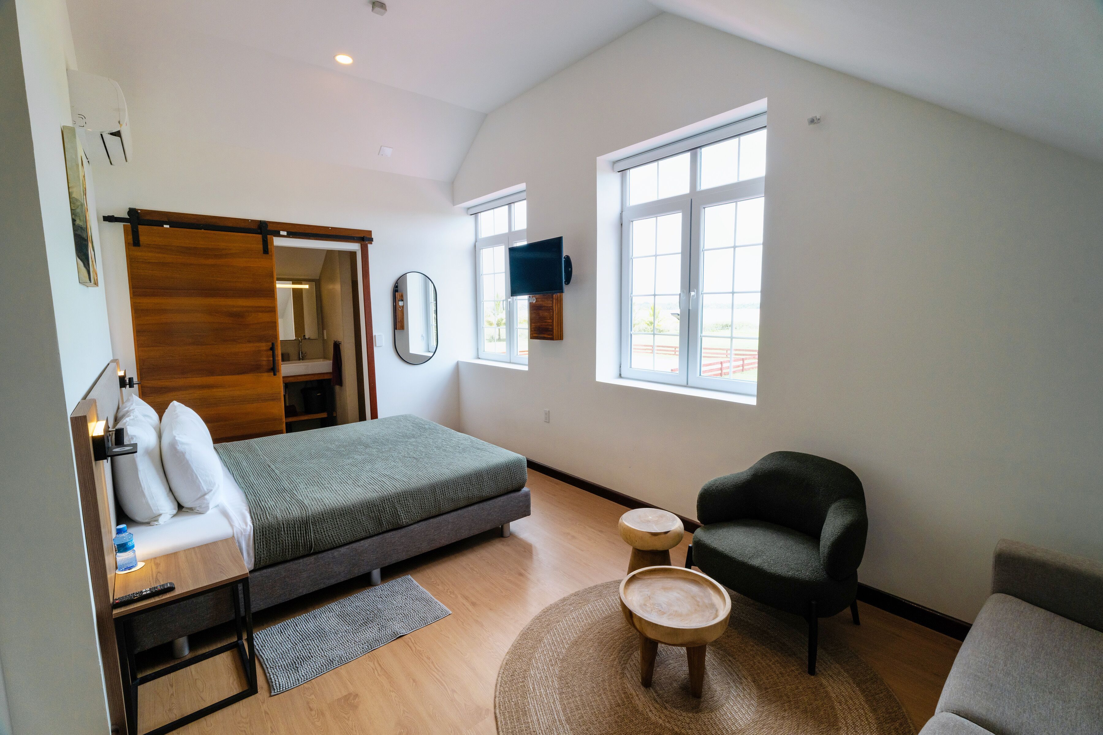 Quarto com uma cama, uma cadeira, uma mesinha, um espelho, uma televisão e uma porta de correr.