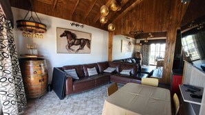 Interior rústico com teto de madeira, um sofá grande, uma mesa de jantar e um barril.